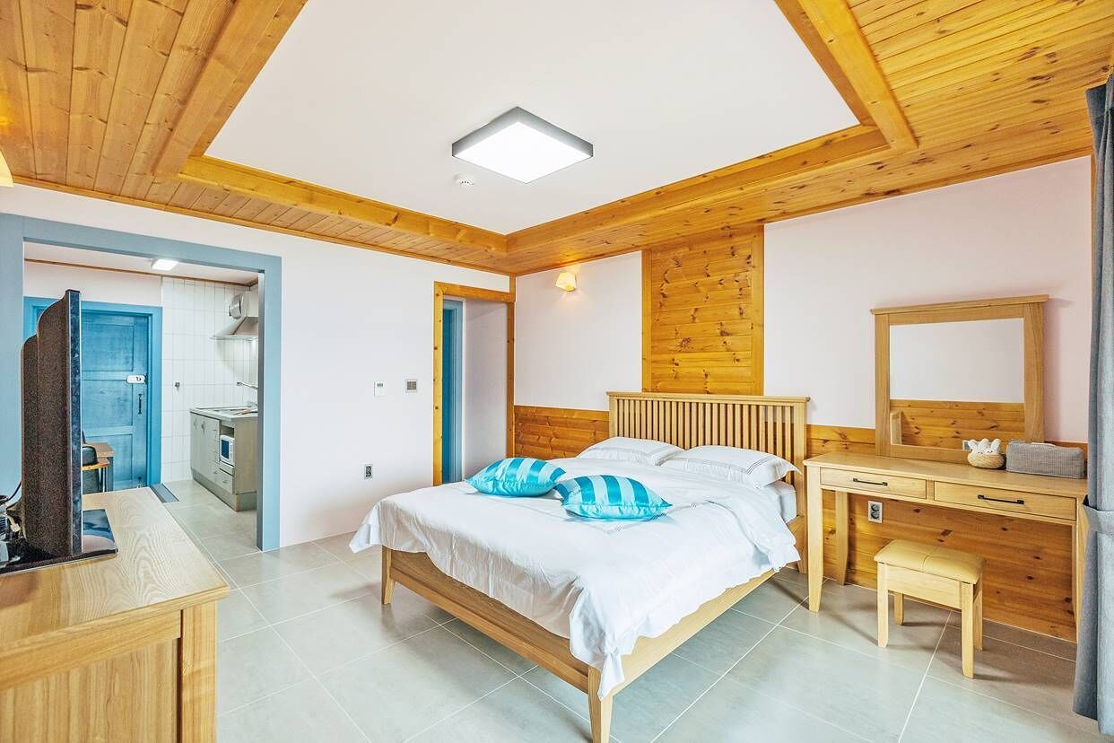 Quarto com teto de madeira, cama com roupa de cama branca, cômoda de madeira e mesa de cabeceira.