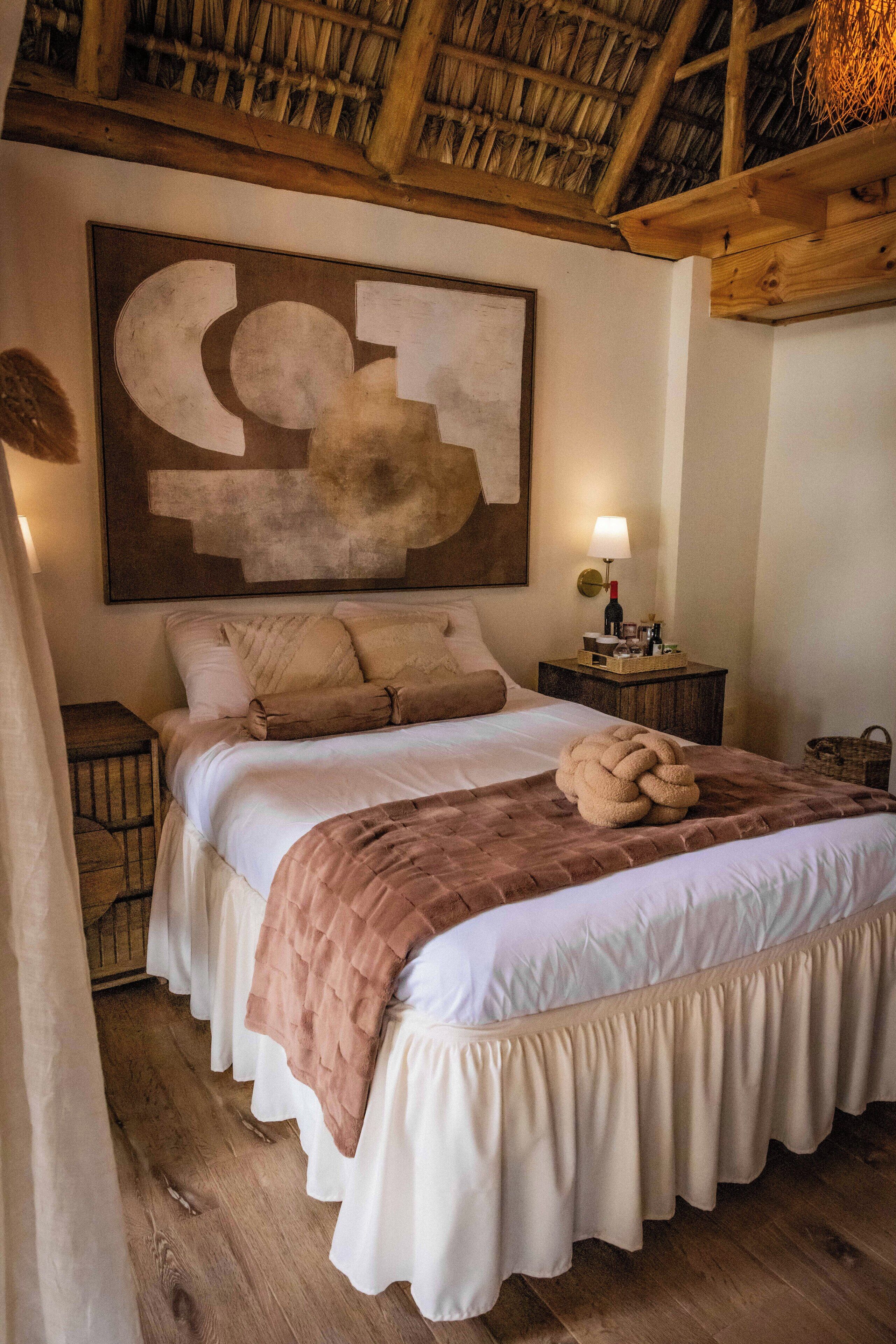 Quarto com uma cama grande, cabeceira de madeira, mesa de cabeceira com abajur e um quadro abstrato na parede.