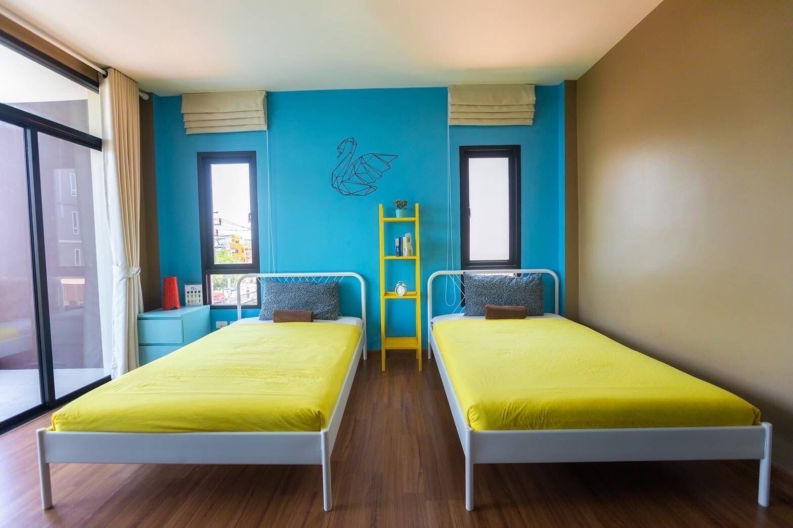 Quarto com duas camas, parede azul e uma janela.