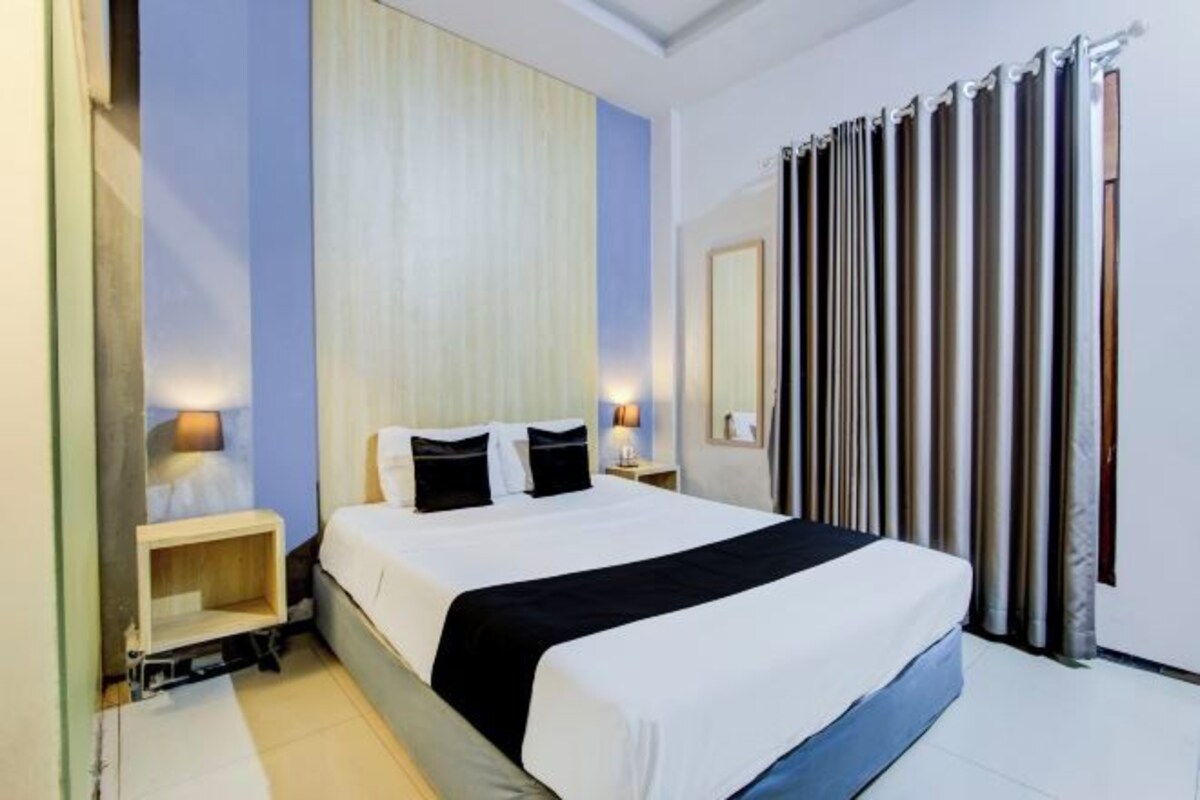 Quarto de hotel com cama, mesas de cabeceira, espelho e cortina.