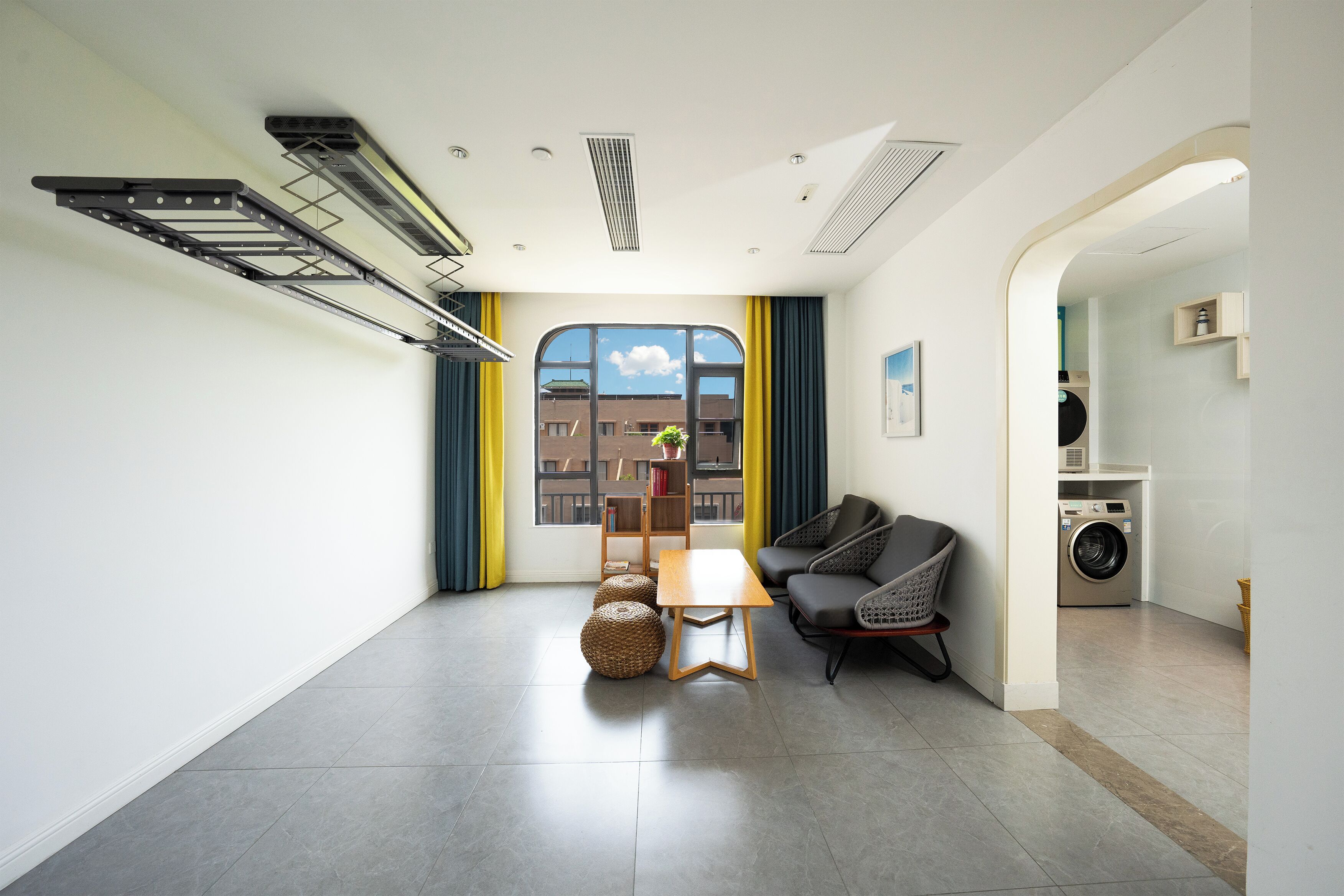 Uma sala de estar moderna com um sofá, uma mesa e uma máquina de lavar ao fundo.