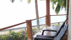 Varanda com duas poltronas de descanso, vista para o mar e um jardim tropical.