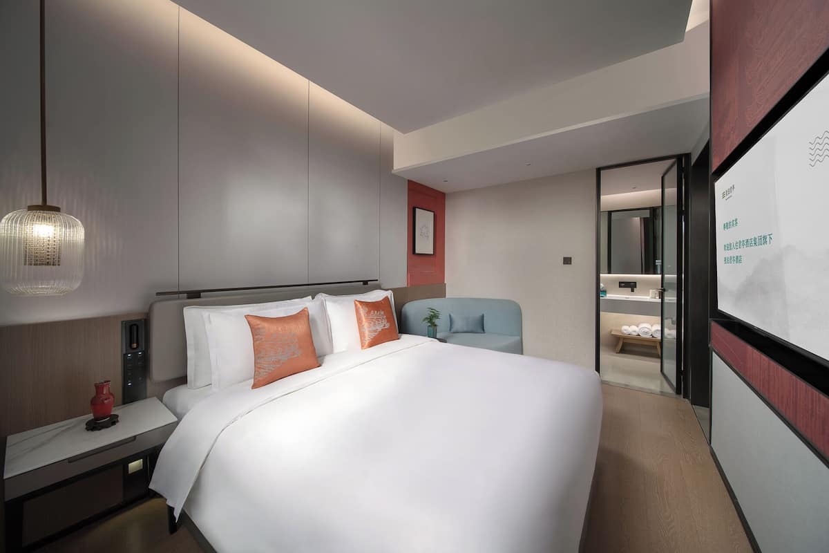 Quarto de hotel moderno com uma cama grande, mesas de cabeceira, escrivaninha e um espaço para sentar.