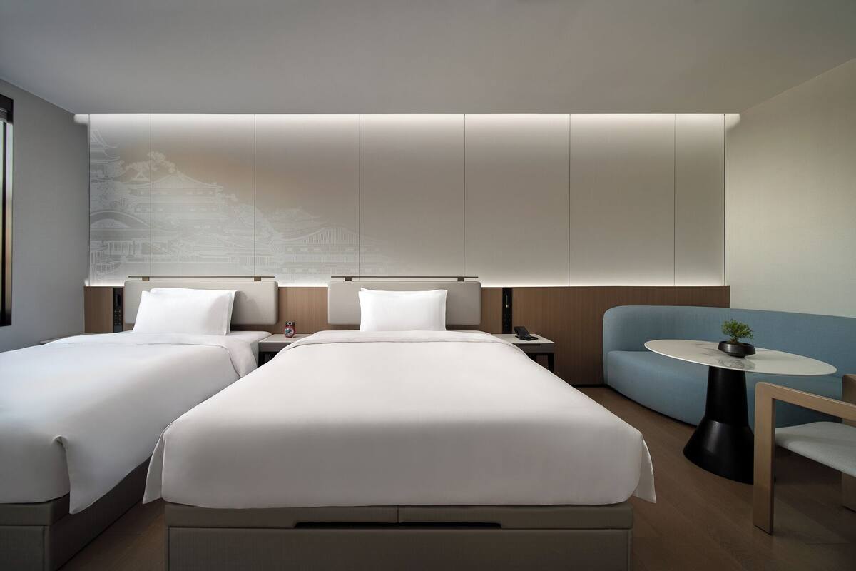 Quarto de hotel moderno com uma cama grande, duas mesas de cabeceira, um sofá e uma pequena mesa redonda.