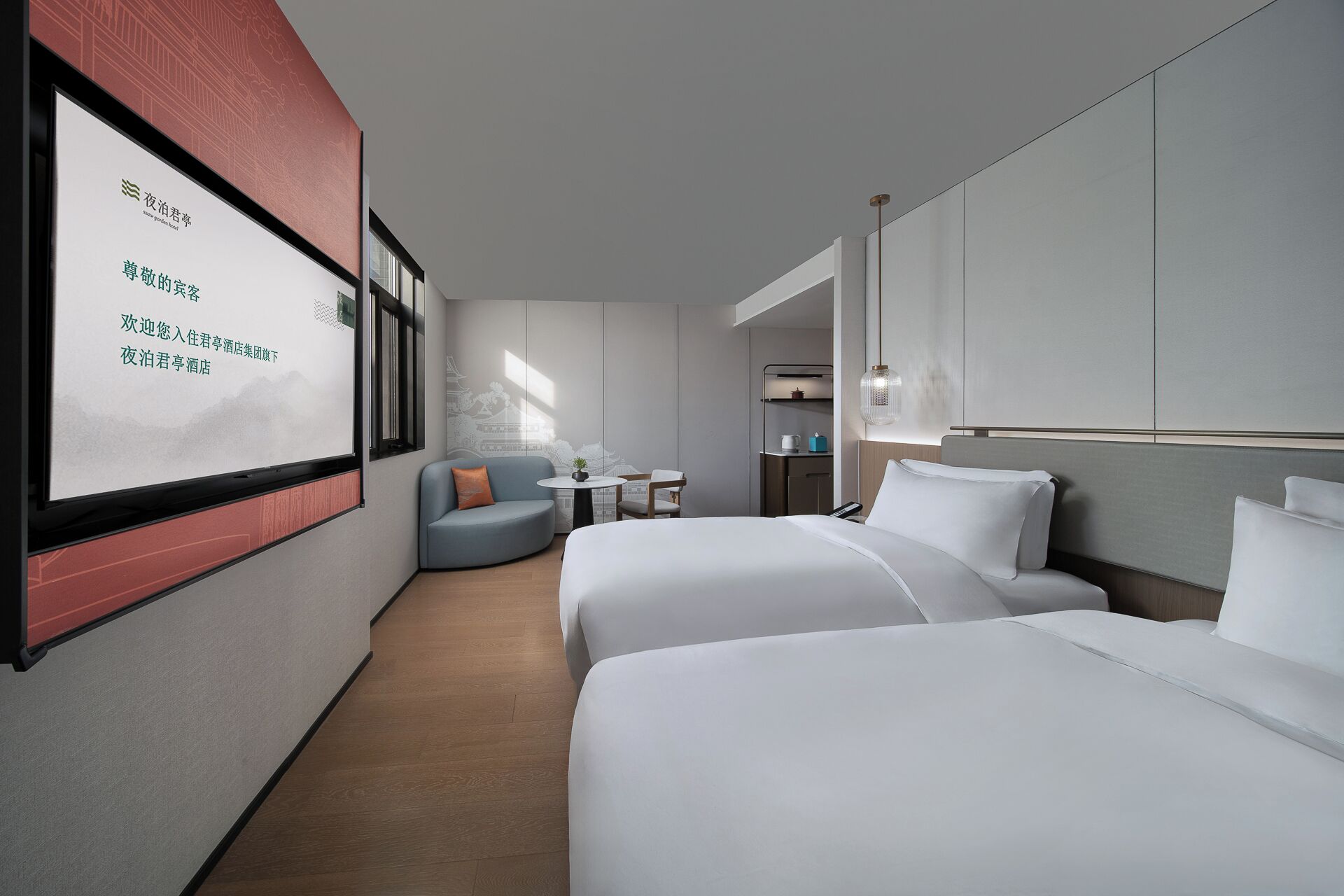 Quarto de hotel moderno com duas camas, área de estar com sofá e cadeiras, uma mesa pequena e uma tela de TV exibindo texto.