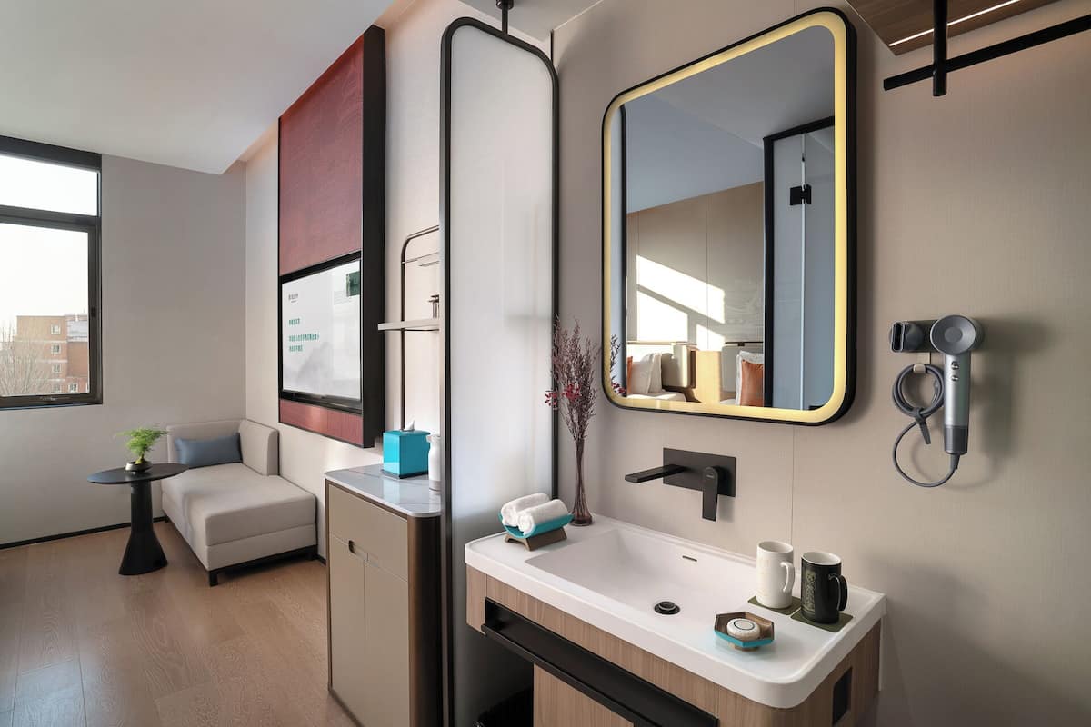 Uma casa de banho moderna com um espelho grande, uma pia com suporte para toalha e um secador de cabelo fixado na parede.