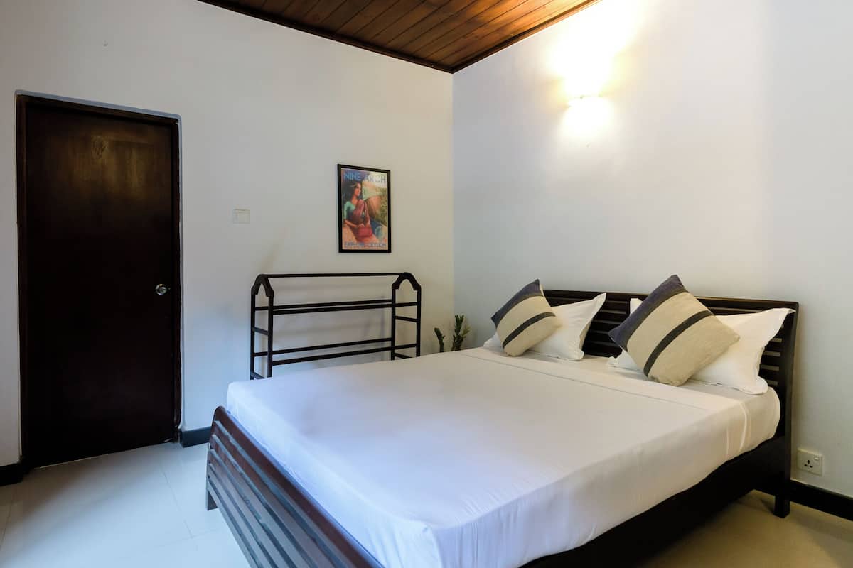 Quarto com cama, porta, luminária fixada na parede e quadro emoldurado.