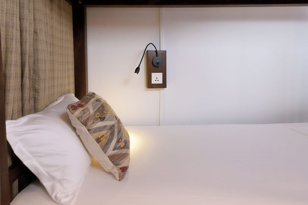 Uma cama bem arrumada com travesseiro estampado, uma tomada na parede e um design de quarto simples e limpo.