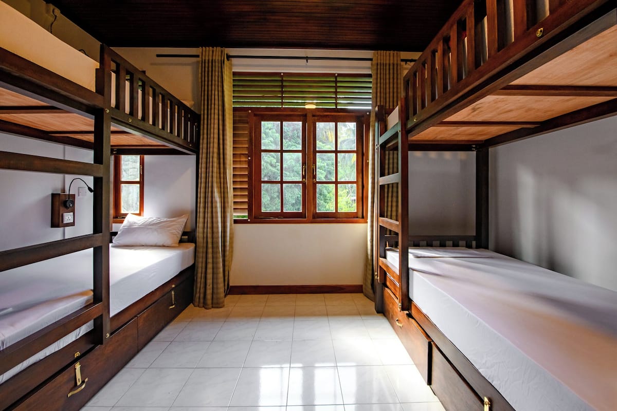 Quarto com beliches, janela com cortinas e teto de madeira.