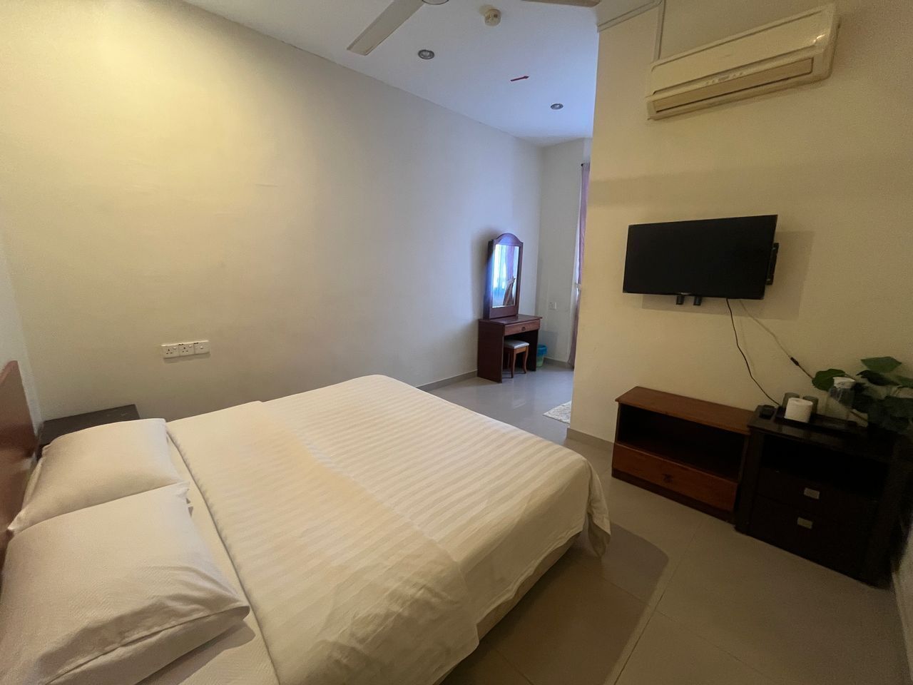 Quarto de hotel com uma cama, televisão na parede, escrivaninha com cadeira e um espelho.