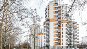 Um edifício residencial com várias andares, varandas, um caminho pavimentado e carros estacionados.