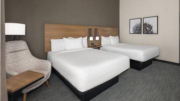 Quarto de hotel com uma cama grande, uma cadeira, uma mesa pequena e duas mesas de cabeceira.