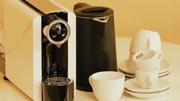 Uma cafeteira, um termo preto e chávenas com pires brancos sobre uma mesa branca.