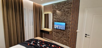 Quarto de hotel moderno com cama, televisão presa a uma parede de mármore e mesa de cabeceira com abajur.