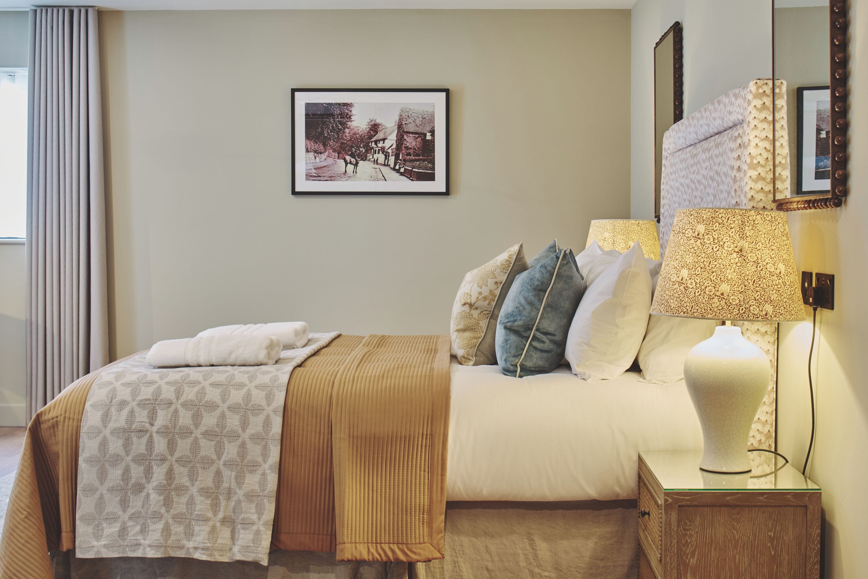 Cama bem arrumada com um edredom estampado, uma luminária de cabeceira e um quadro na parede.
