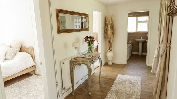 Quarto com cama, mesa de cabeceira, abajur, vaso com flores e espelho.