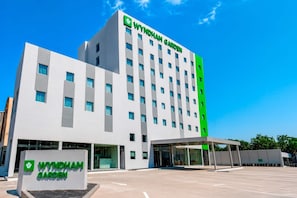 Edifício moderno de hotel com esquema de cores verde e branco marcante, apresentando uma entrada ampla e um céu claro.