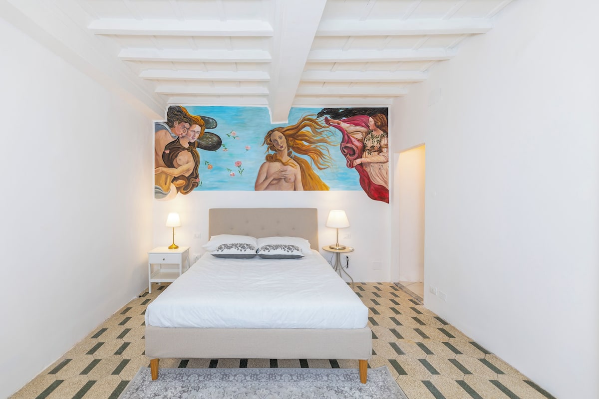 Um quarto com uma cama, duas mesas de cabeceira, um mural grande na parede e um piso estampado.