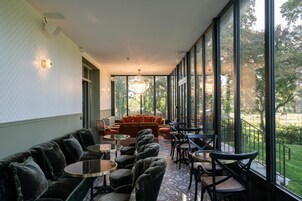 Amplo espaço interno com um longo banco, várias mesas e cadeiras. Grandes janelas oferecem vista para o exterior.