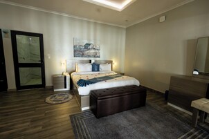 Um quarto moderno com uma cama, mesas de cabeceira, um banco, cômoda e um quadro na parede.