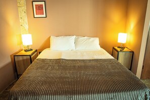 Quarto de hotel com cama, duas luminárias de cabeceira e um quadro pendurado na parede.