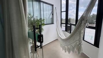 Quarto com rede, cadeira, planta em vaso e vista através de amplas janelas.