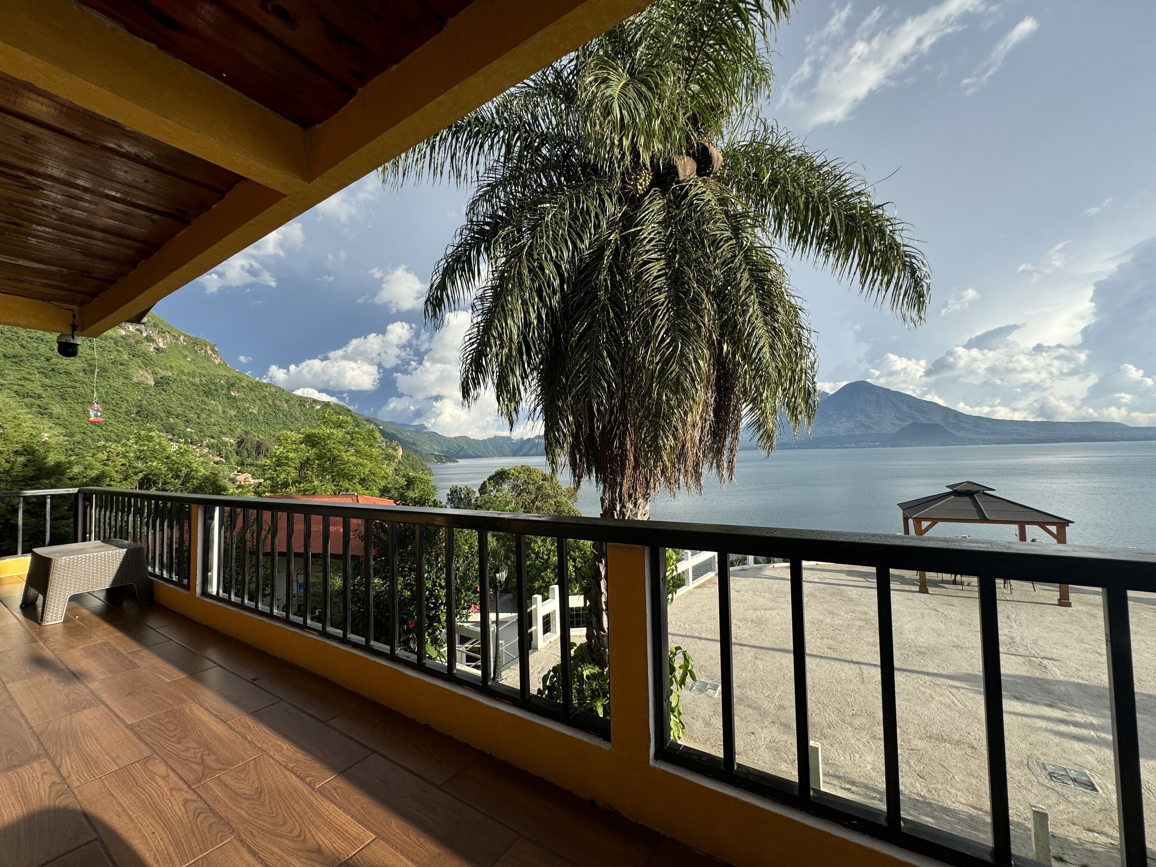 Uma varanda com vista para um lago, uma palmeira e uma montanha ao fundo.