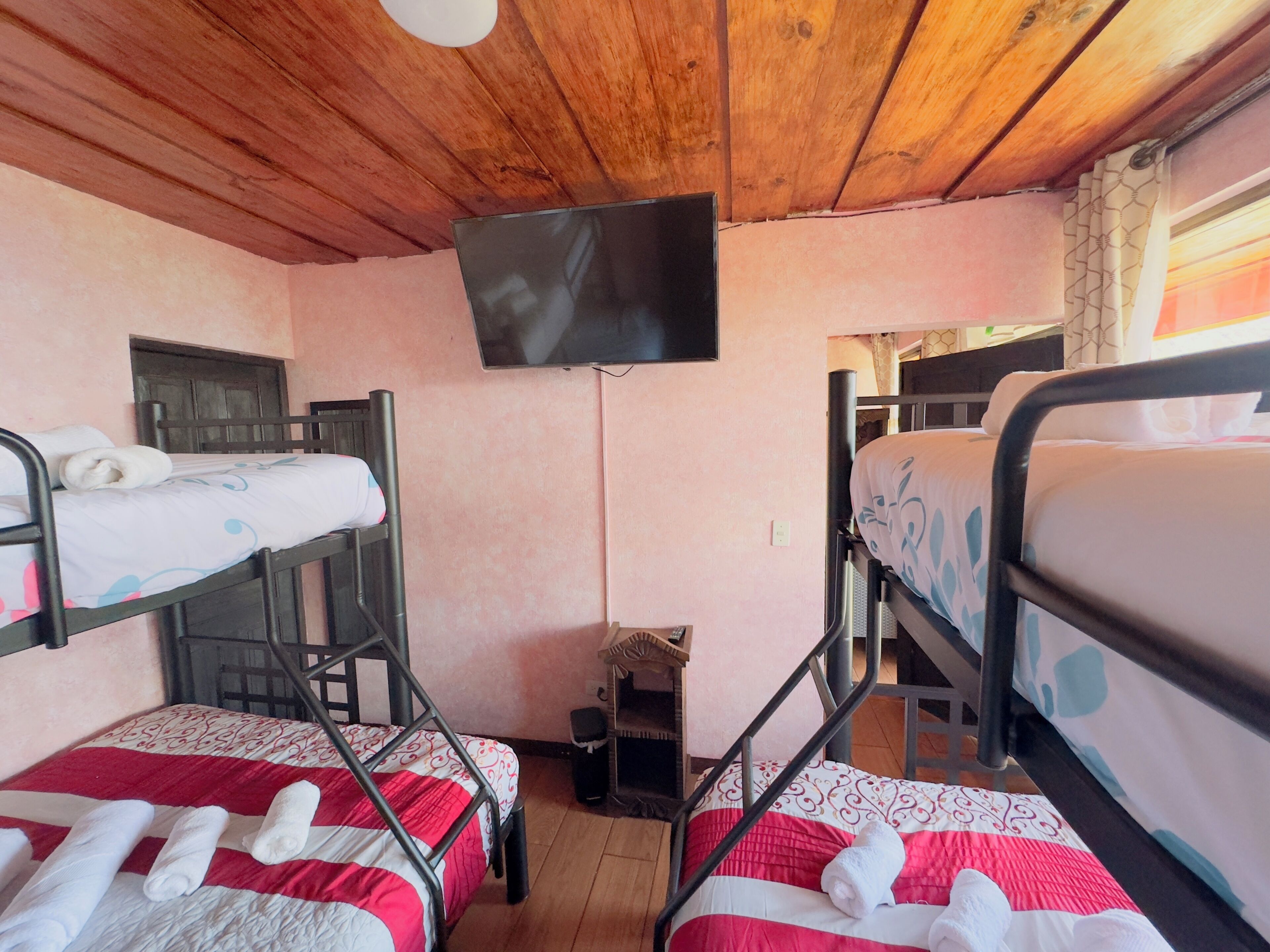 Quarto com beliches, televisão fixada na parede e uma pequena lixeira.