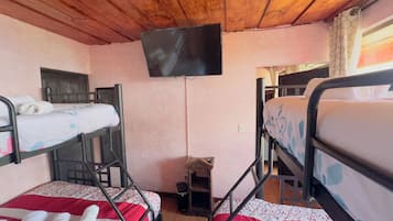 Quarto com beliches, televisão fixada na parede e uma pequena lixeira.