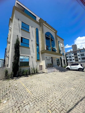 Um edifício moderno com uma grande janela em arco, fachada branca e entrada com calçada.