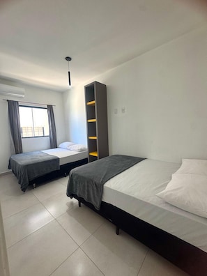 Quarto de hotel com duas camas, um guarda-roupa e uma janela com cortinas.