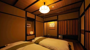 Quarto japonês tradicional com duas camas, vigas de madeira, piso de tatame e um lampião de papel pendurado.