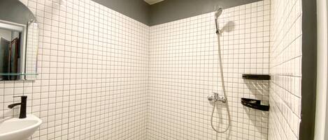 Casa de banho com canto, revestida a azulejos brancos tipo metrô, prateleira de vidro, pia e chuveiro com chuveiro manual.