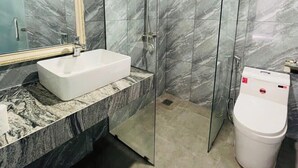 Um banheiro moderno com chuveiro em box de vidro, pia branca e vaso sanitário.