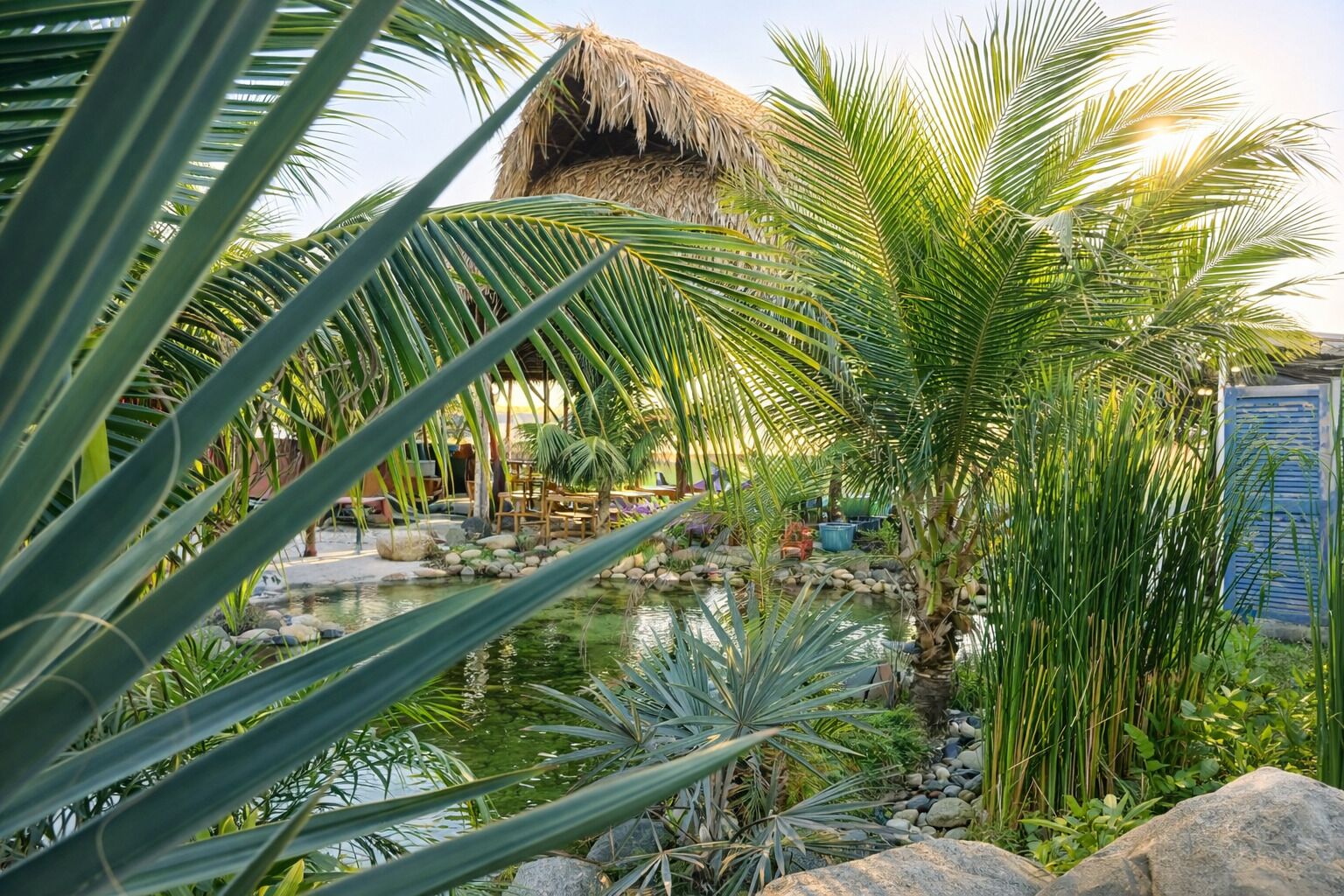 Um jardim tropical com lago, palmeiras e uma estrutura de colmo.