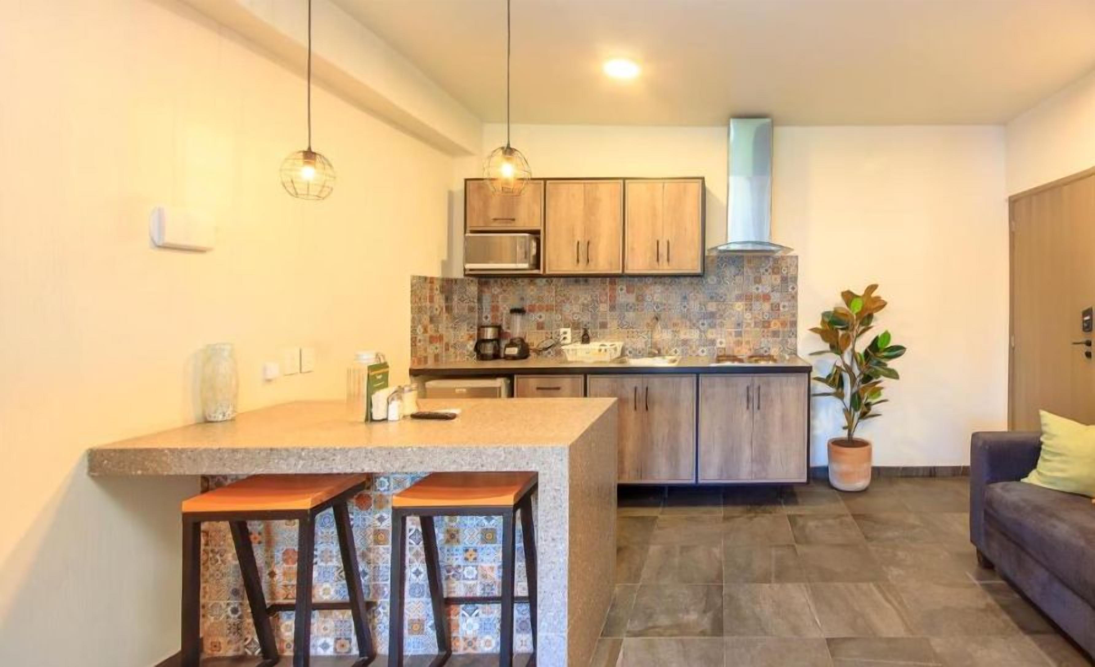Uma cozinha compacta com ilha central, armários de madeira e luminárias pendentes.