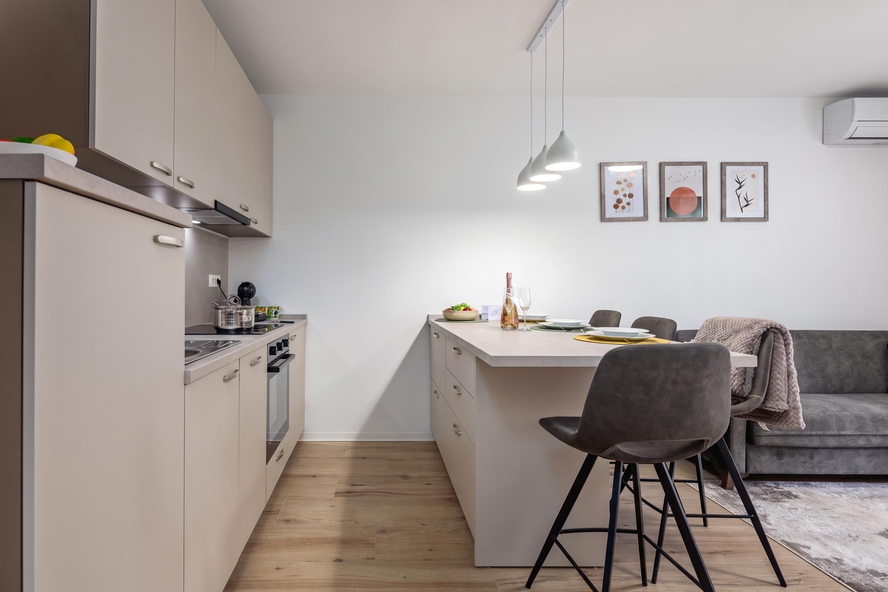 Cozinha moderna com ilha central, área de jantar com sofá cinza e parede com três obras de arte emolduradas.