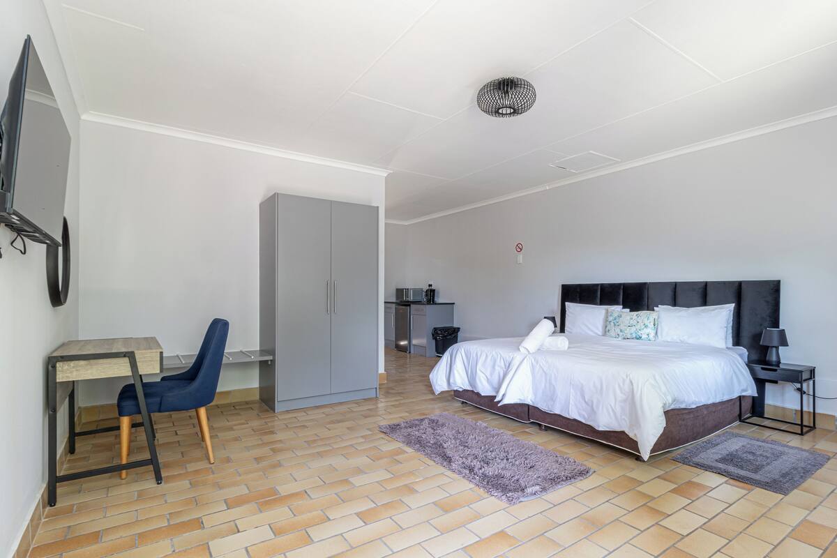 Quarto com cama, escrivaninha e cadeira. Cozinha compacta ao fundo.