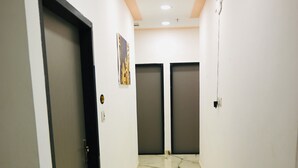 Corredor com piso de mármore, paredes brancas e duas portas fechadas.