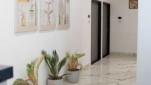 Um corredor com piso de mármore, plantas em vasos e três obras de arte botânicas emolduradas na parede.