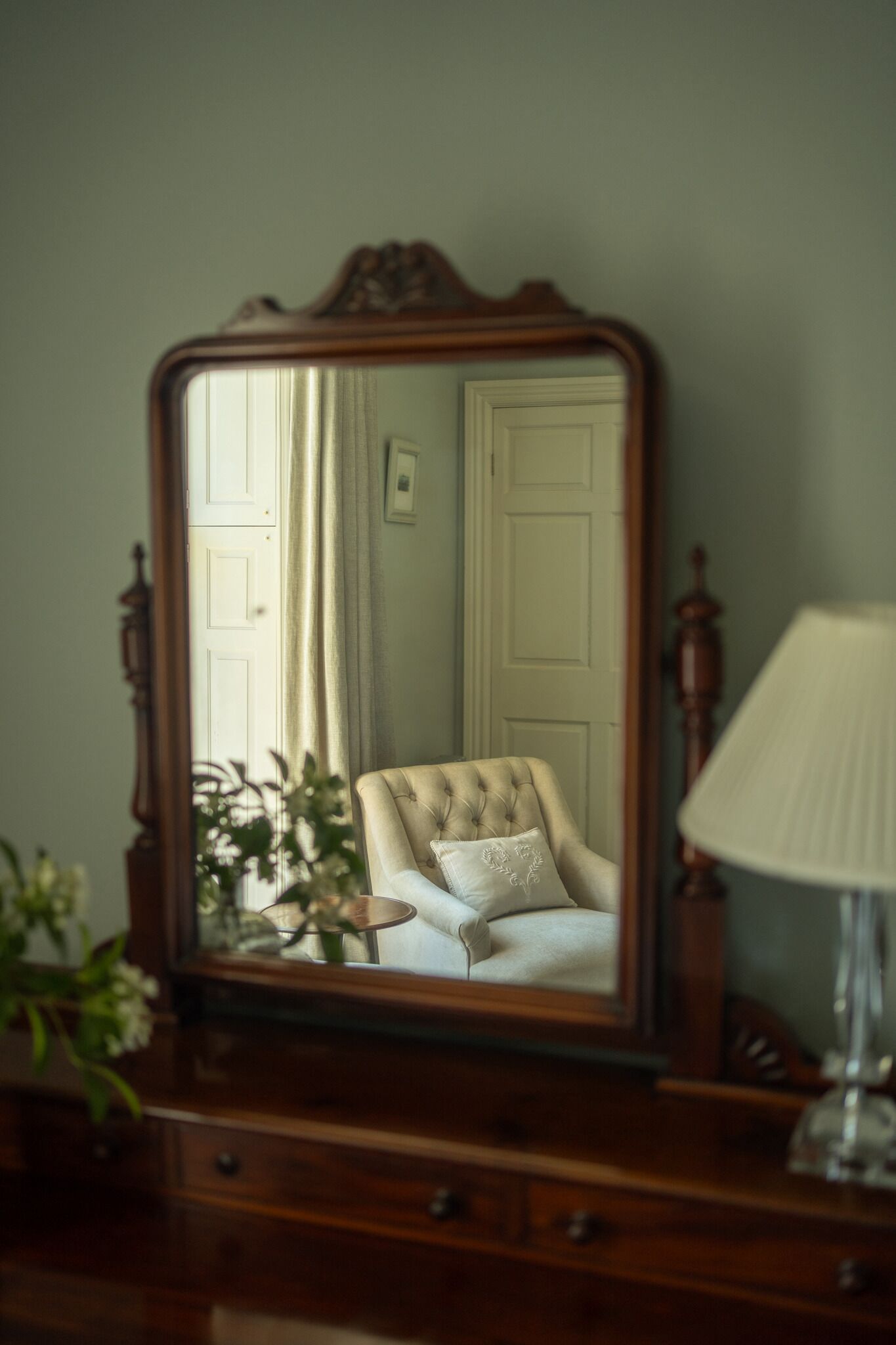 Um espelho reflete um quarto com uma cadeira, uma luminária e um penteado.