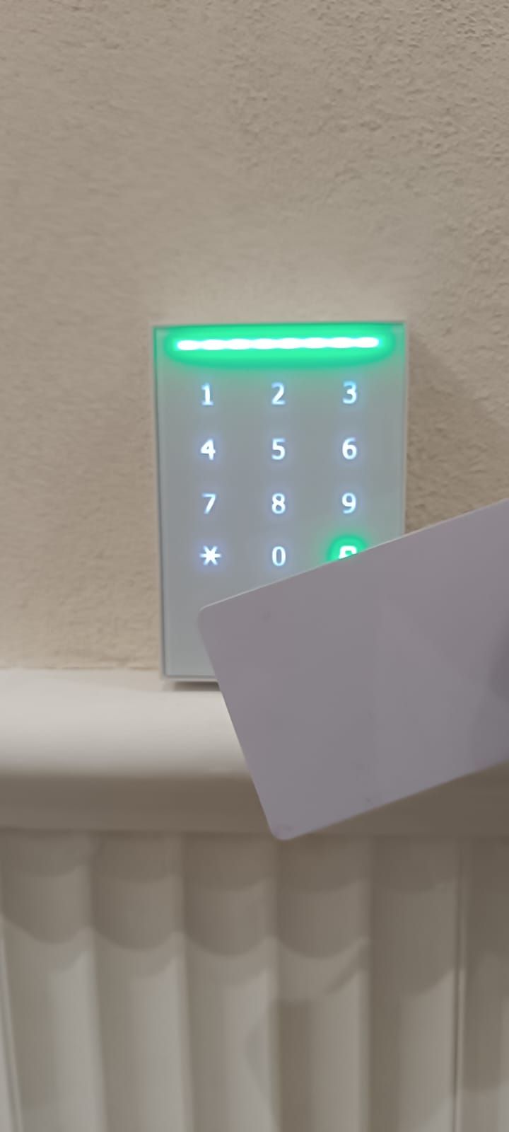 Um painel de teclas numéricas iluminadas e uma luz verde na parte superior, fixado na parede.