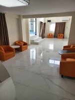 Um quarto amplo, com piso de mármore, poltronas laranja, uma pequena mesa redonda e uma escada que dá acesso a outra área.