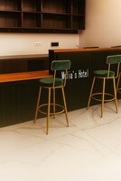 Uma mesa de recepção com uma placa indicando "Mr. Lia's Hotel" e dois banquetas estofadas verdes com pés dourados.