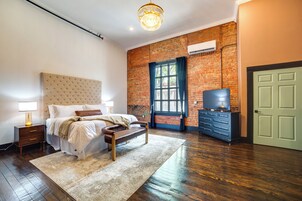 Quarto com cama grande, penteadeira, televisão e parede de tijolos.