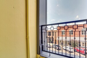 Janela com grade de metal dando para uma rua com carros estacionados e edifícios.