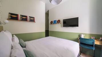 Quarto de hotel com cama, uma secretária com cadeira, televisão de tela plana e obras de arte nas paredes.