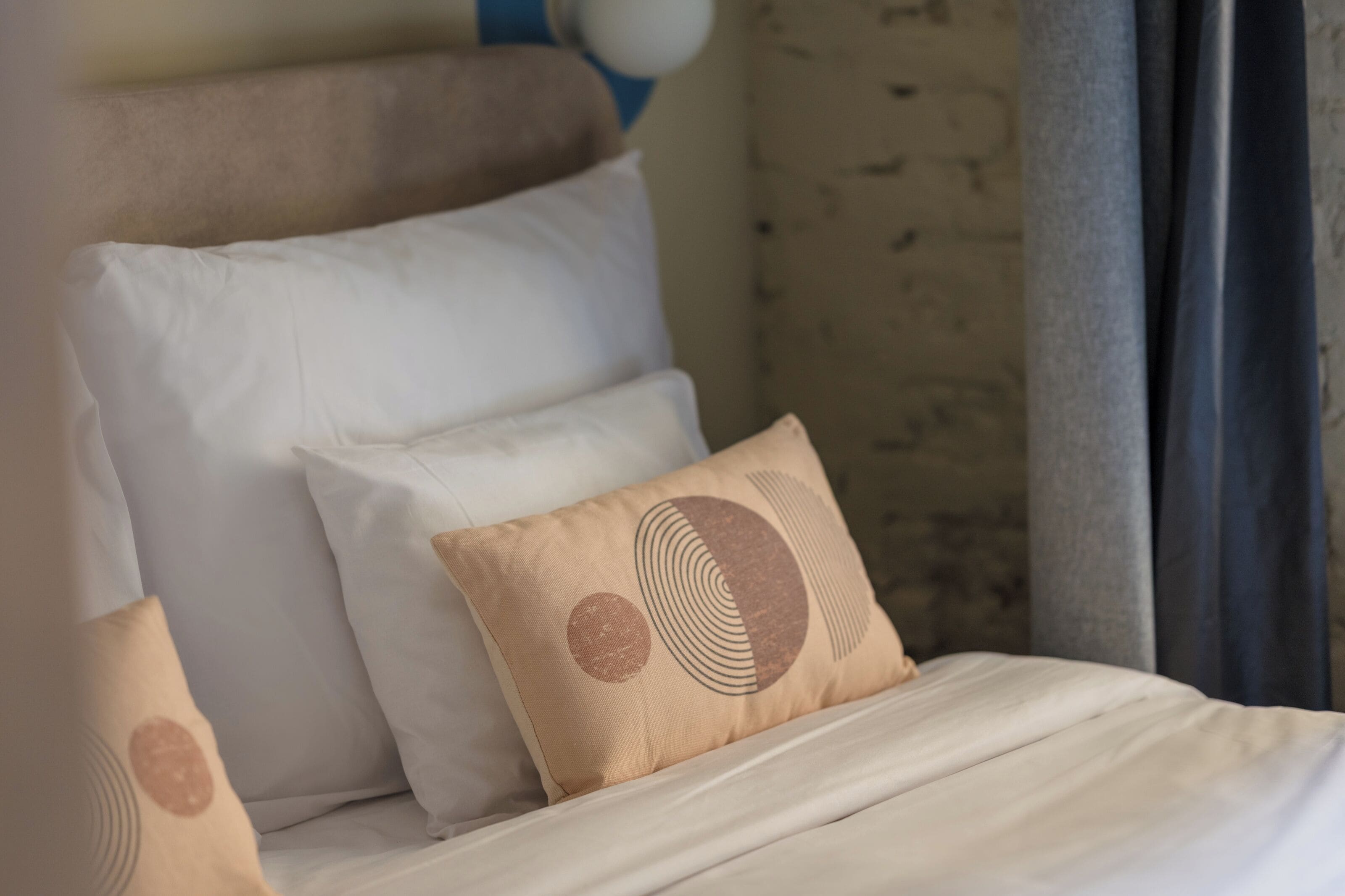 Cama com roupa de cama branca e dois travesseiros bege com desenhos circulares.