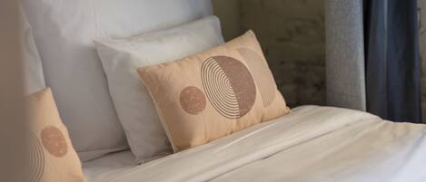 Cama com roupa de cama branca e dois travesseiros bege com desenhos circulares.