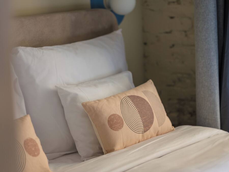 Cama com roupa de cama branca e dois travesseiros bege com desenhos circulares.